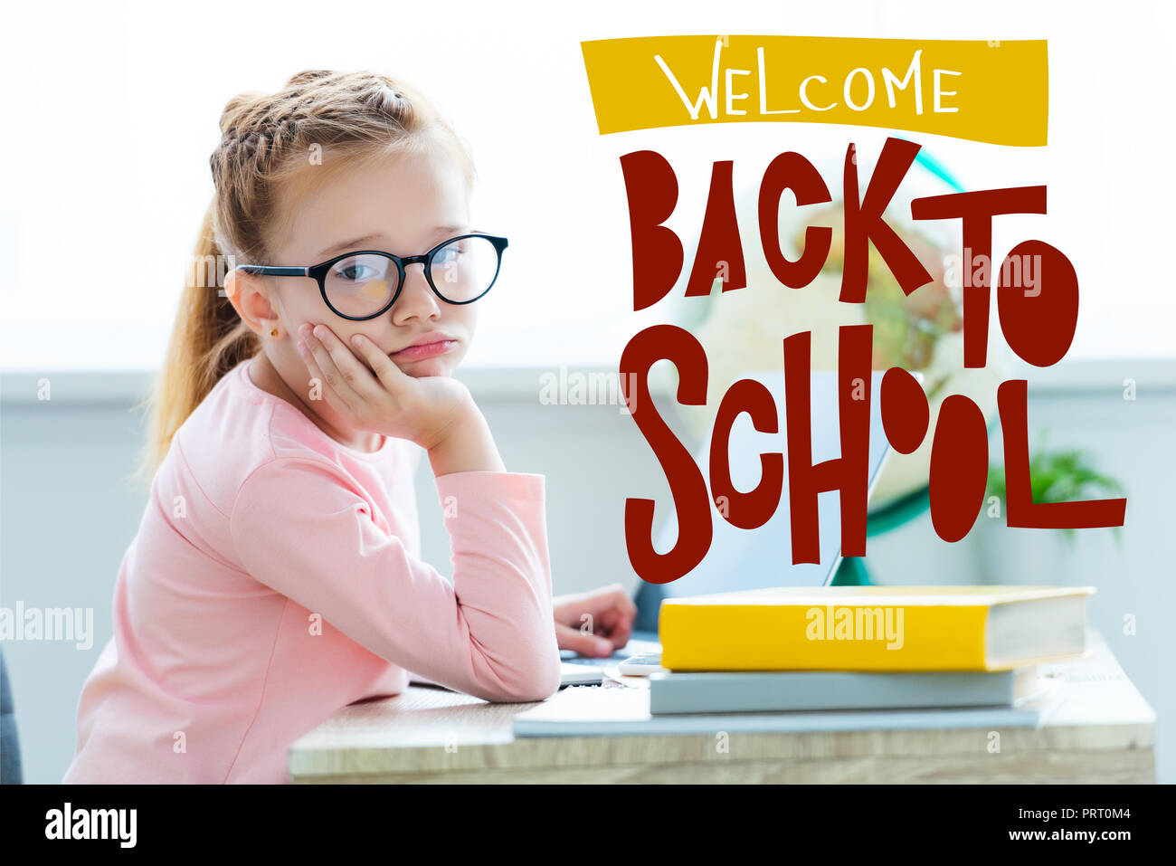 Bored child in eyeglasses looking at camera while studying with laptop ...
