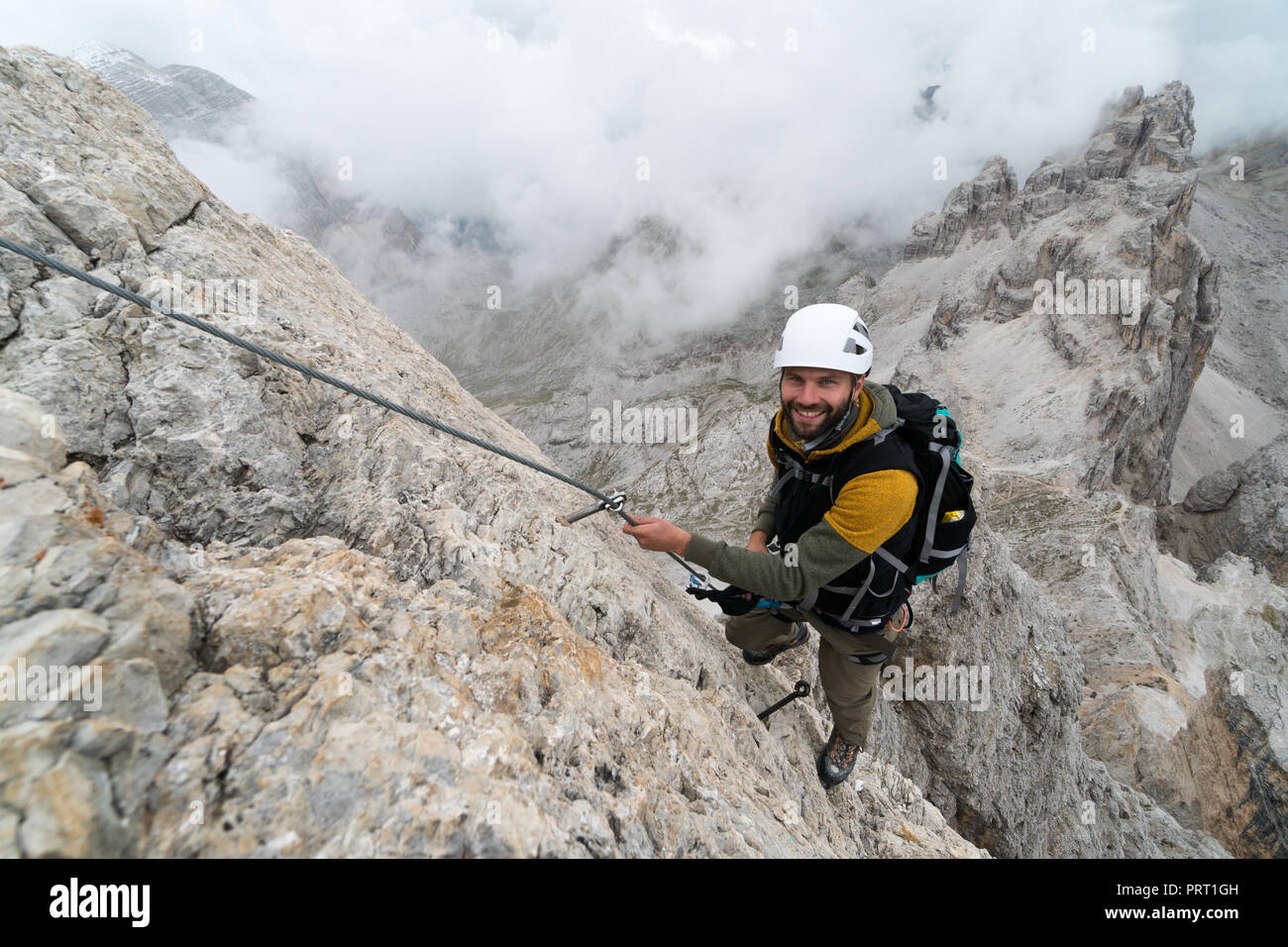 young male climber on a steep and exposed rock face climbing a Via ...