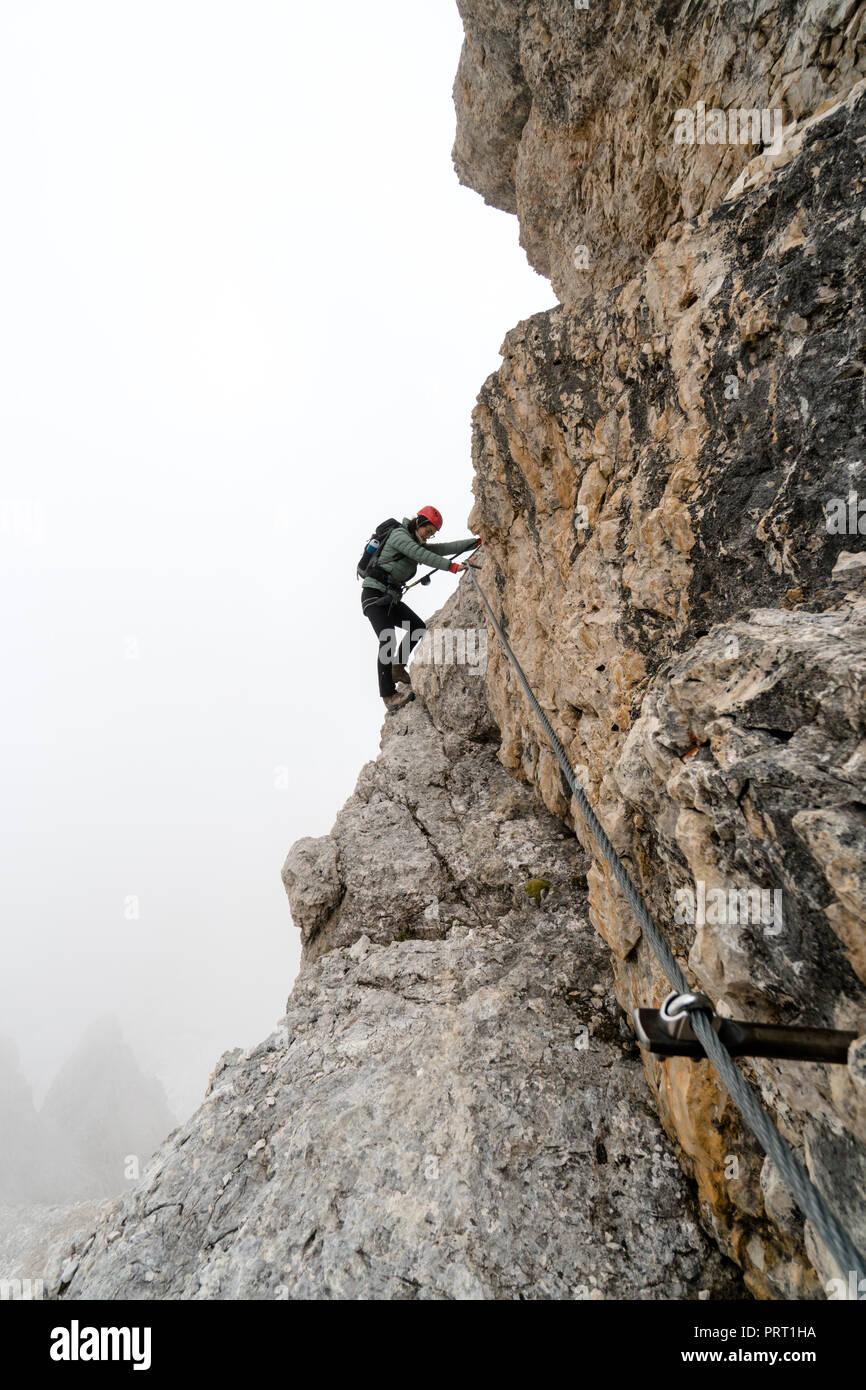 young female climber on a vertical and exposed rock face climbing a Via ...