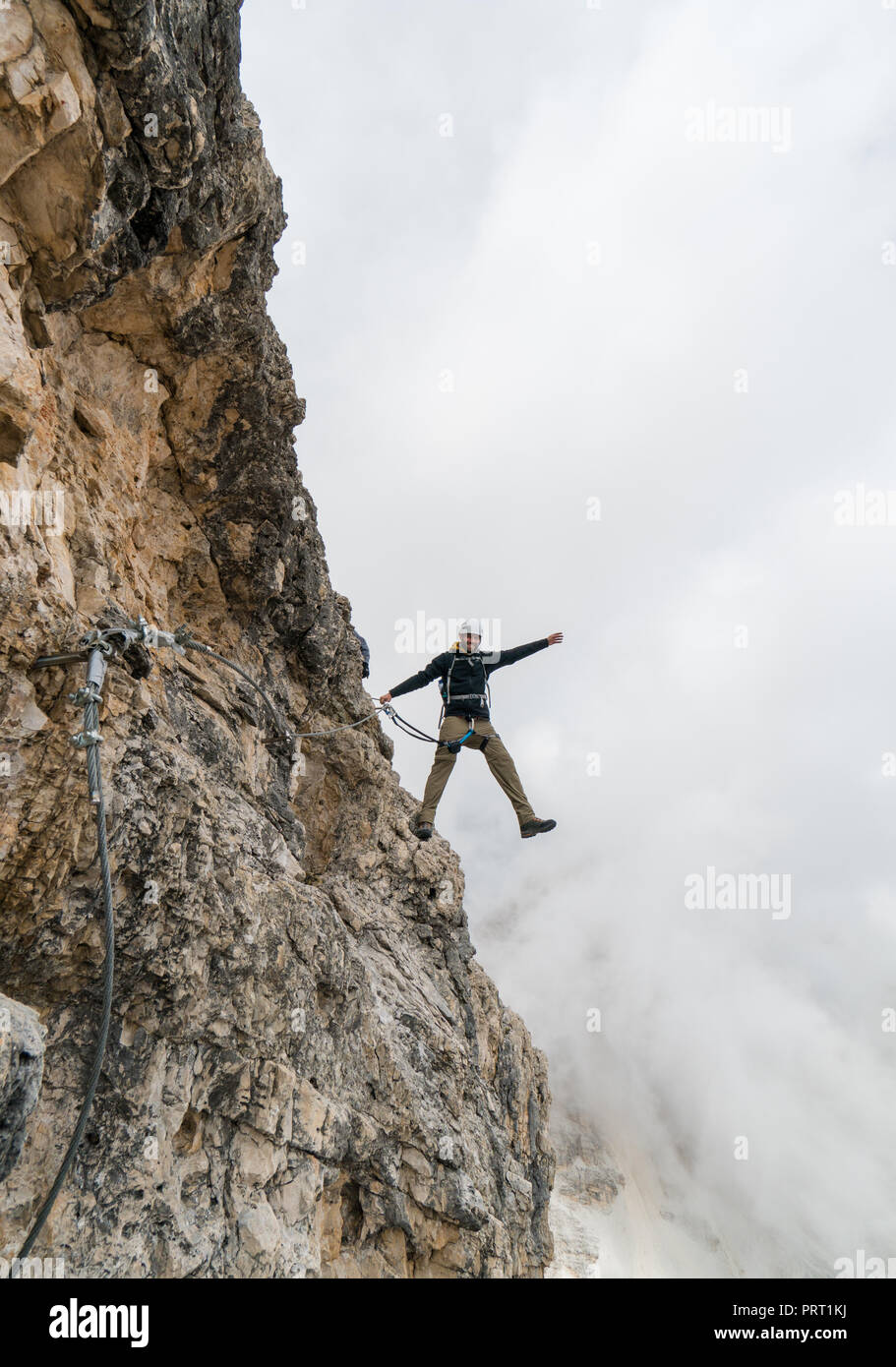 young male climber on a steep and exposed rock face climbing a Via ...