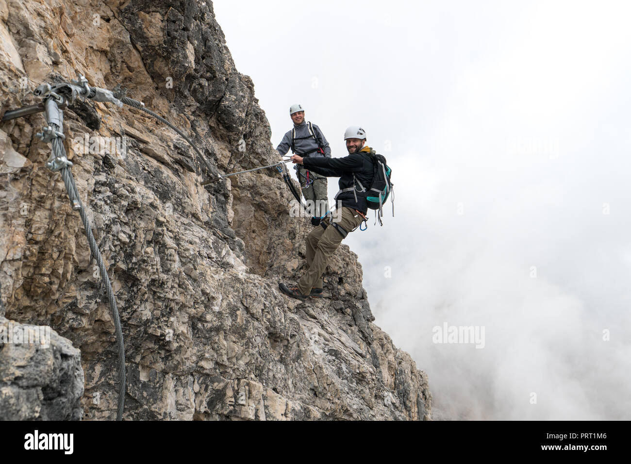 young climbers on a steep and exposed rock face climbing a Via Ferrata ...