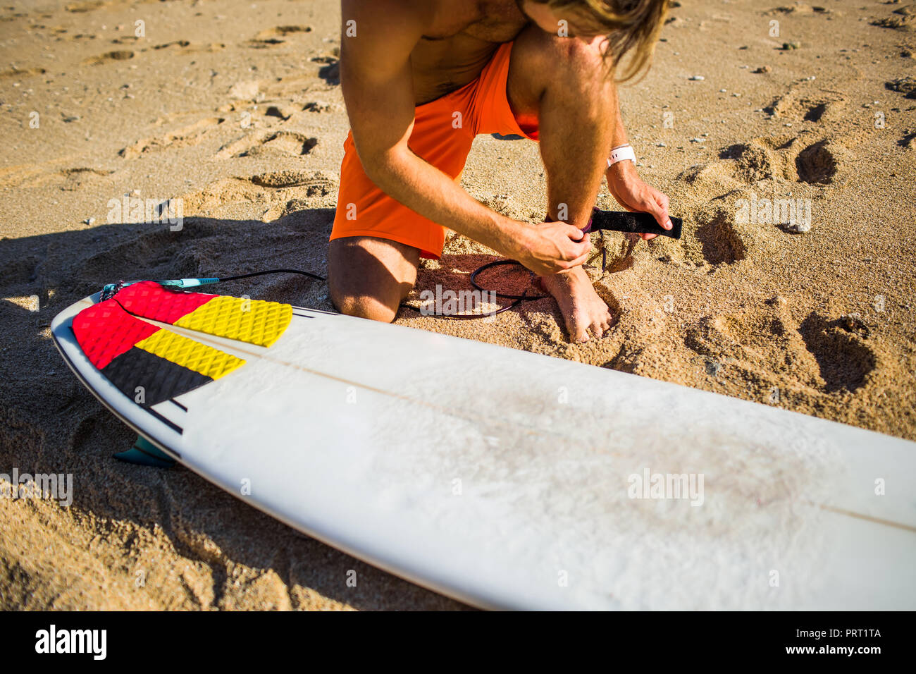partial view of sportsman getting ready for surfing on sandy beach ...