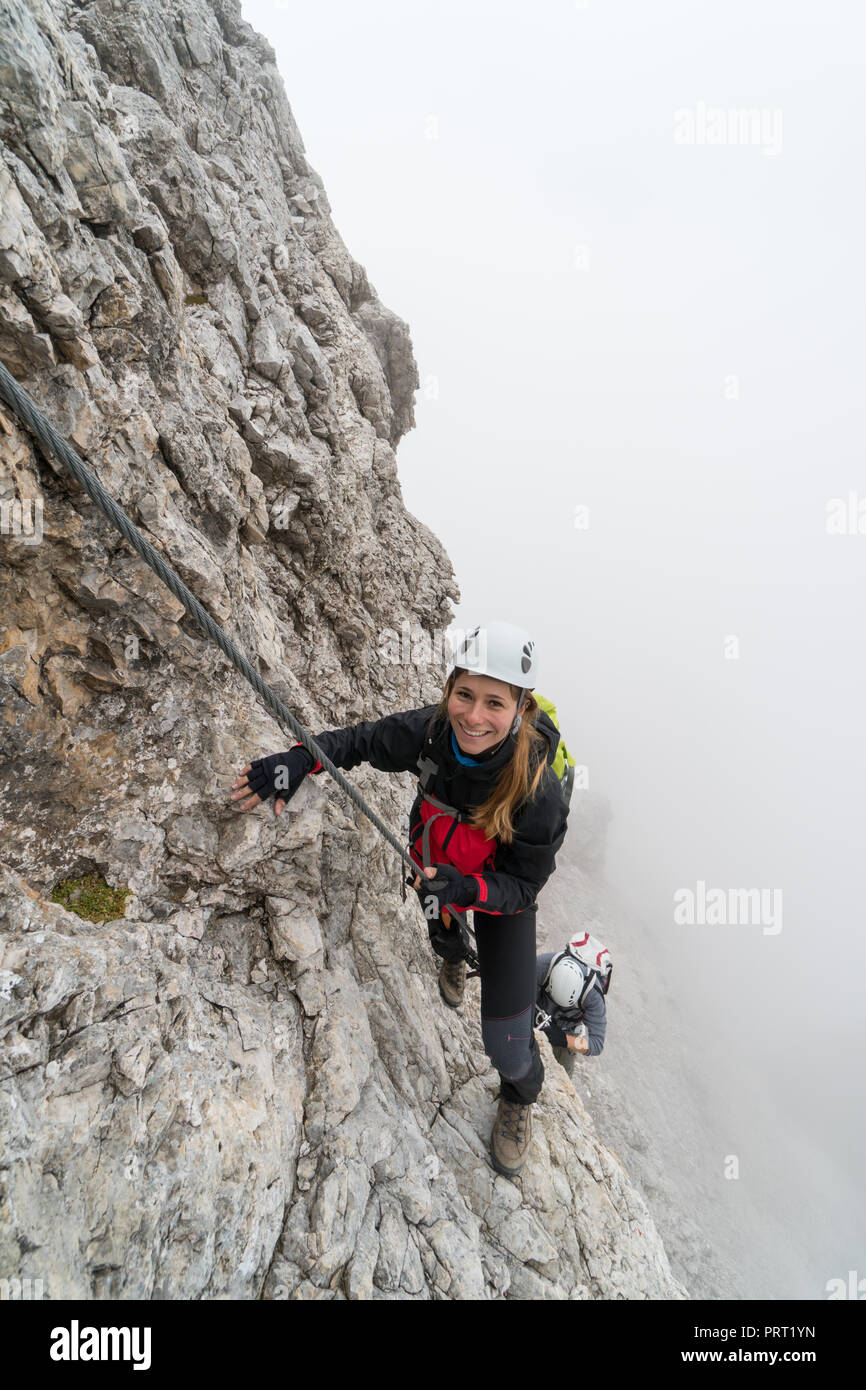 young attractive climbers on a vertical and exposed rock face climbs a ...