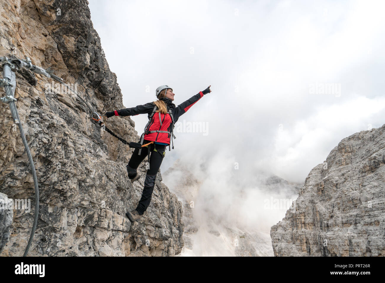 young female climber on a vertical and exposed rock face smiling and ...