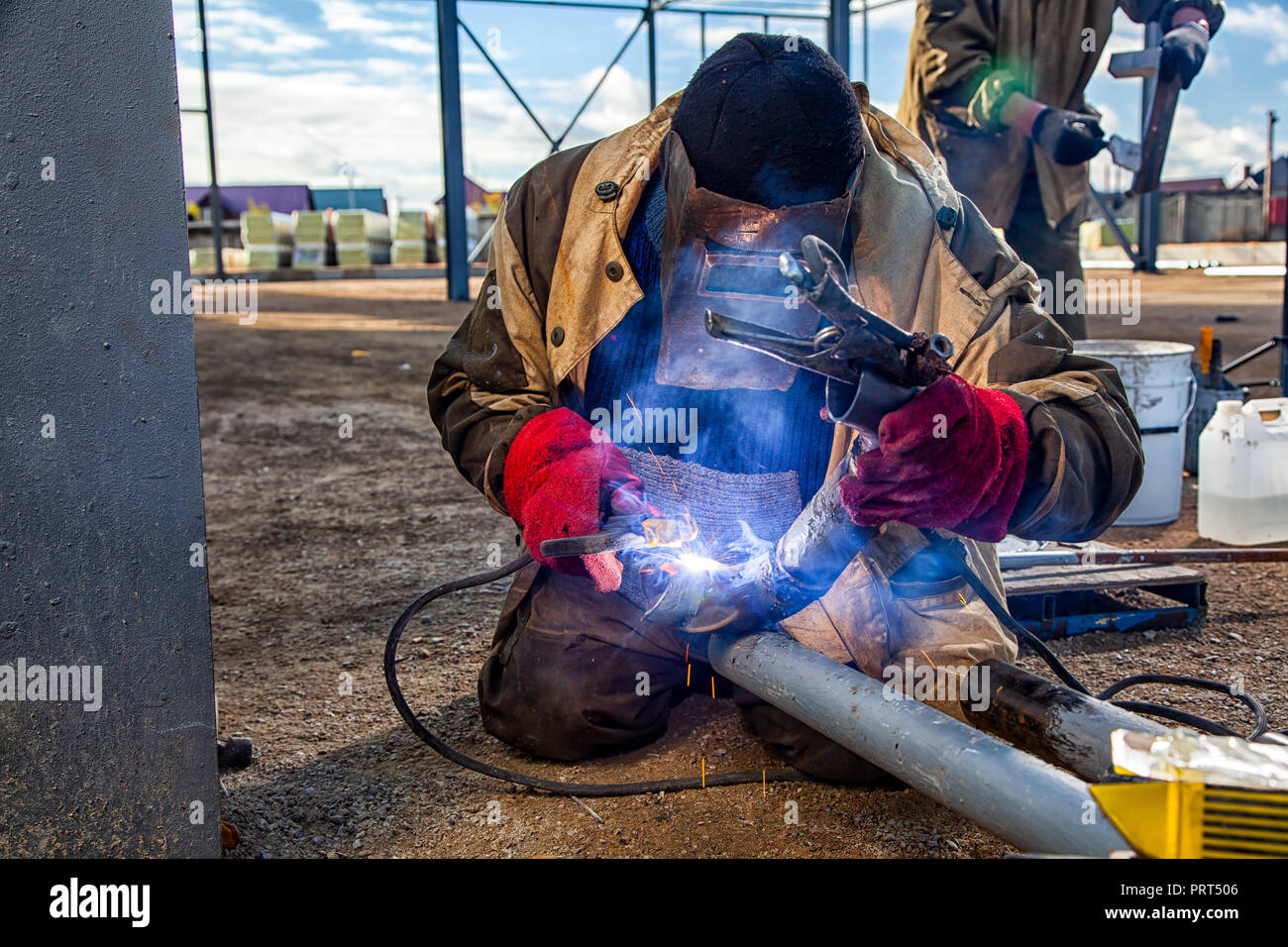 A strong man is a welder in brown uniform, welding mask and welders ...