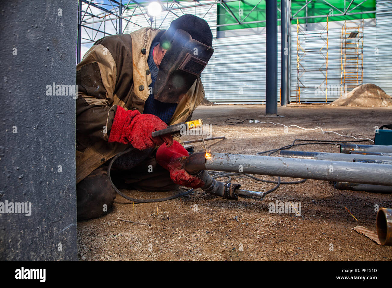 A builder welder in brown working clothes welds a metal product with arc welding machine in the ...