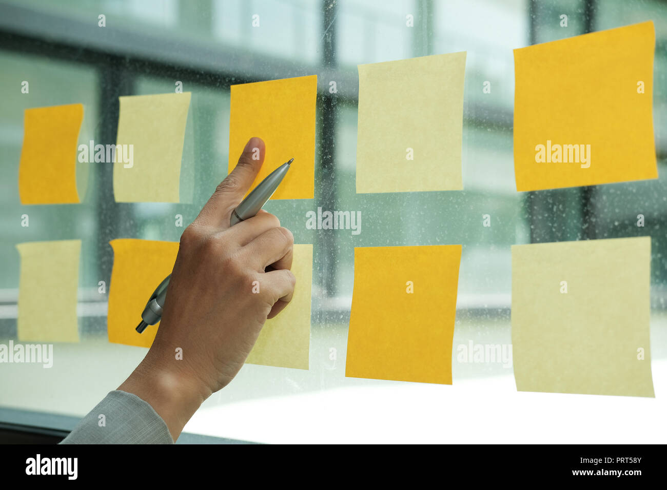 hand pointing at adhesive notes on glass wall at workplace. Sticky note ...