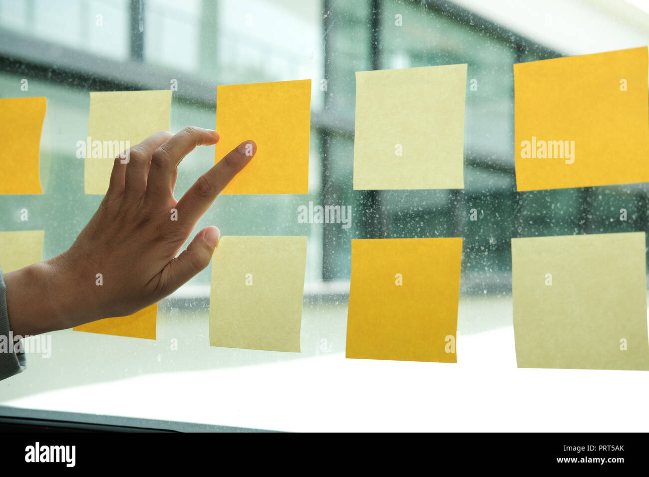 hand pointing at adhesive notes on glass wall at workplace. Sticky note ...