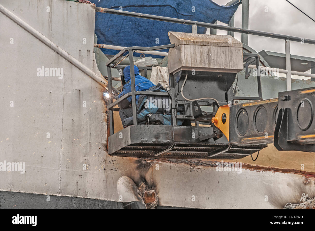 welder at work on a ship sitting in a cage of a crane welding a steel ...
