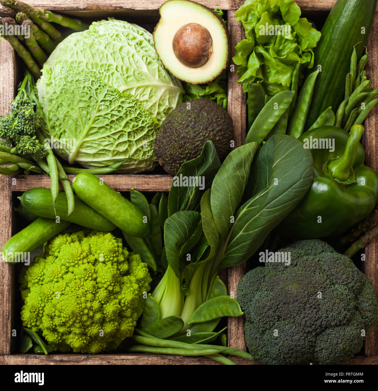 Assorted green toned raw organic vegetables in wooden box on dark stone ...