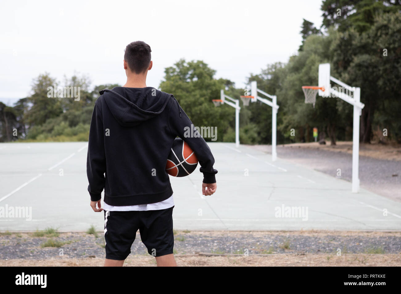 Male teenage basketball player looking out over basketball court, rear ...