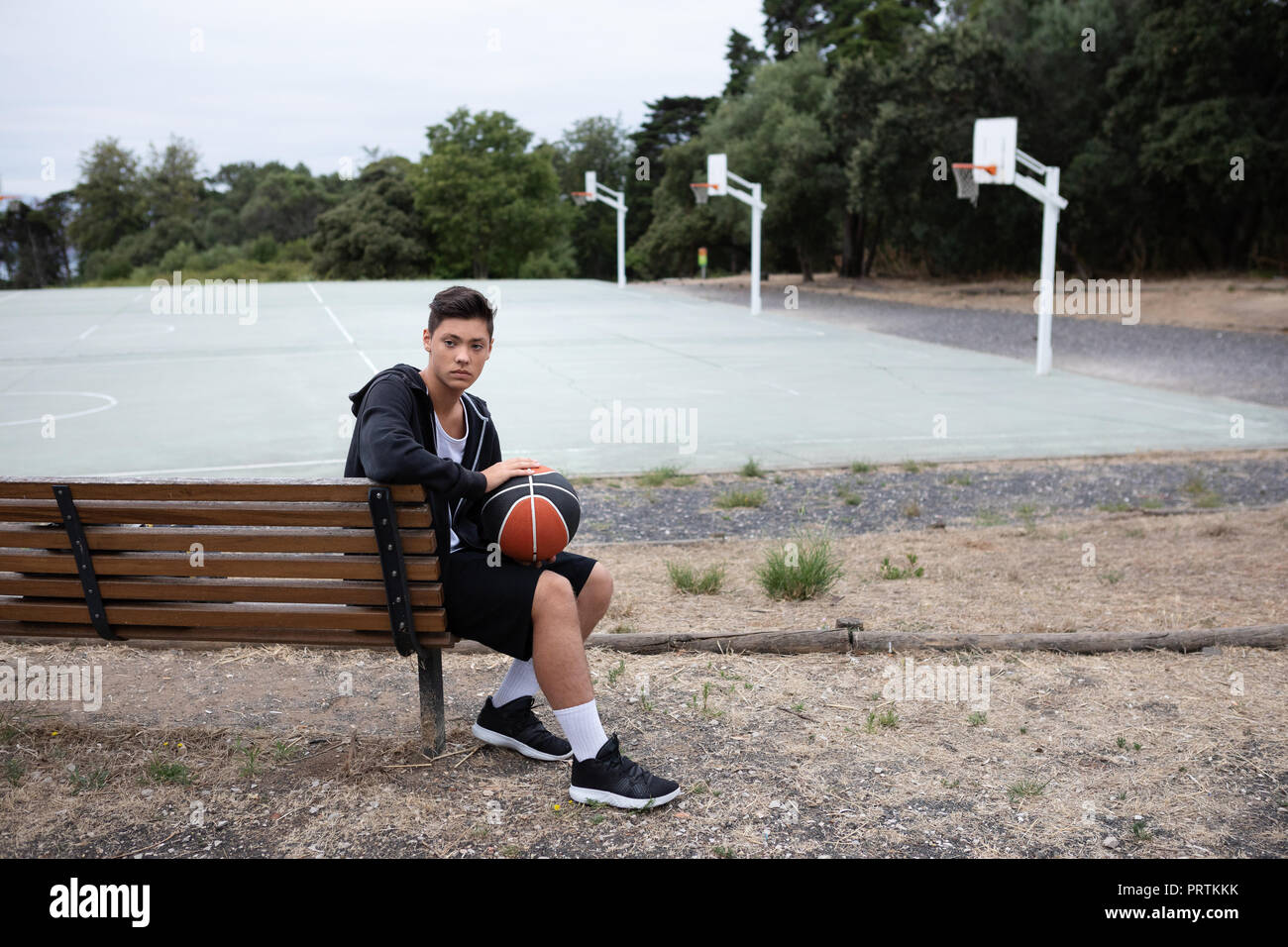 Male teenage basketball player sitting on park bench by basketball ...