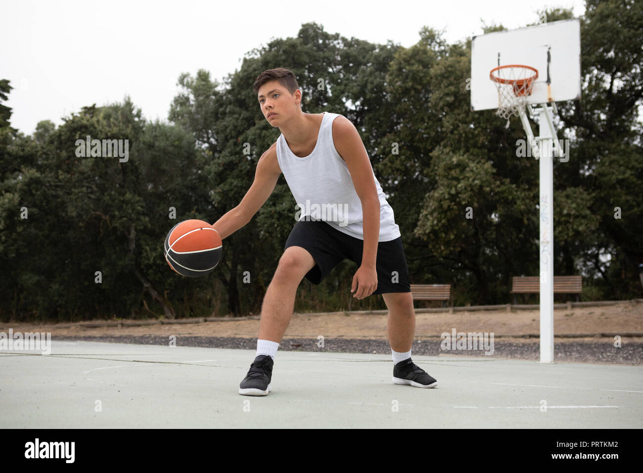 Male teenage basketball player playing basketball on court Stock Photo ...