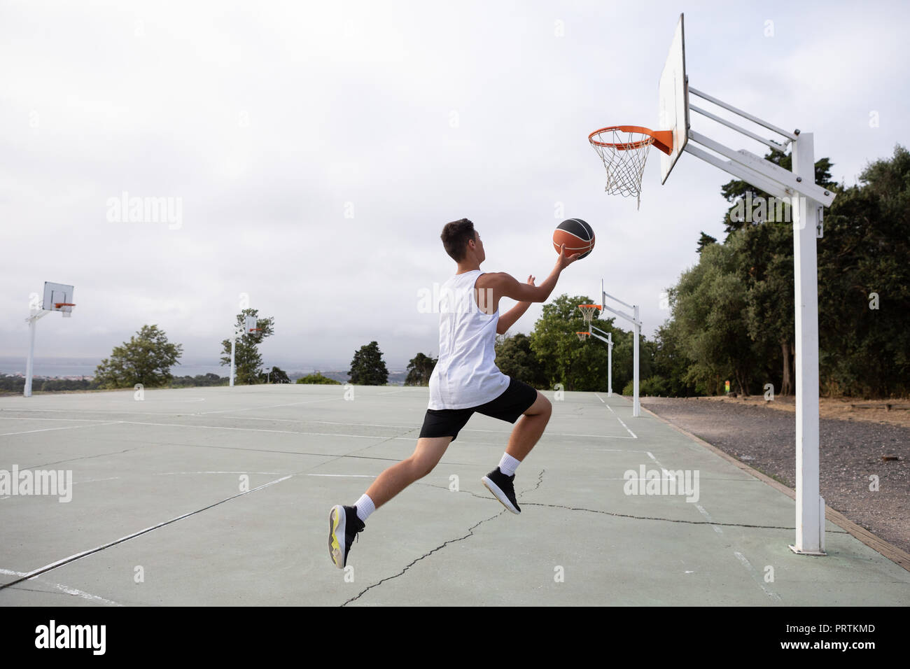 Male teenage basketball player jumping with ball toward basketball hoop ...