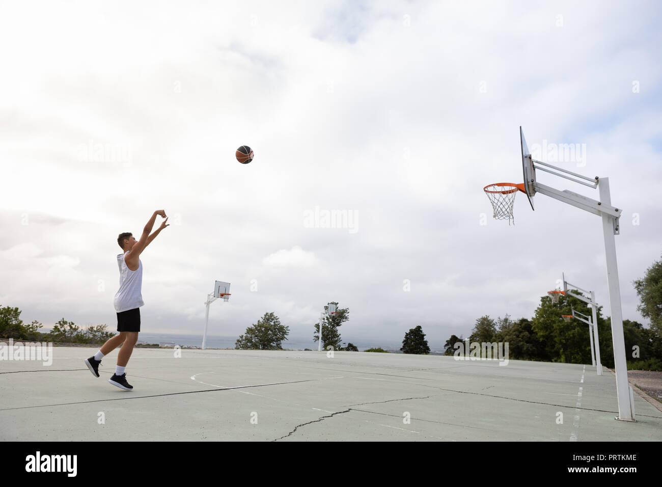 Male teenage basketball player throwing ball toward basketball hoop ...