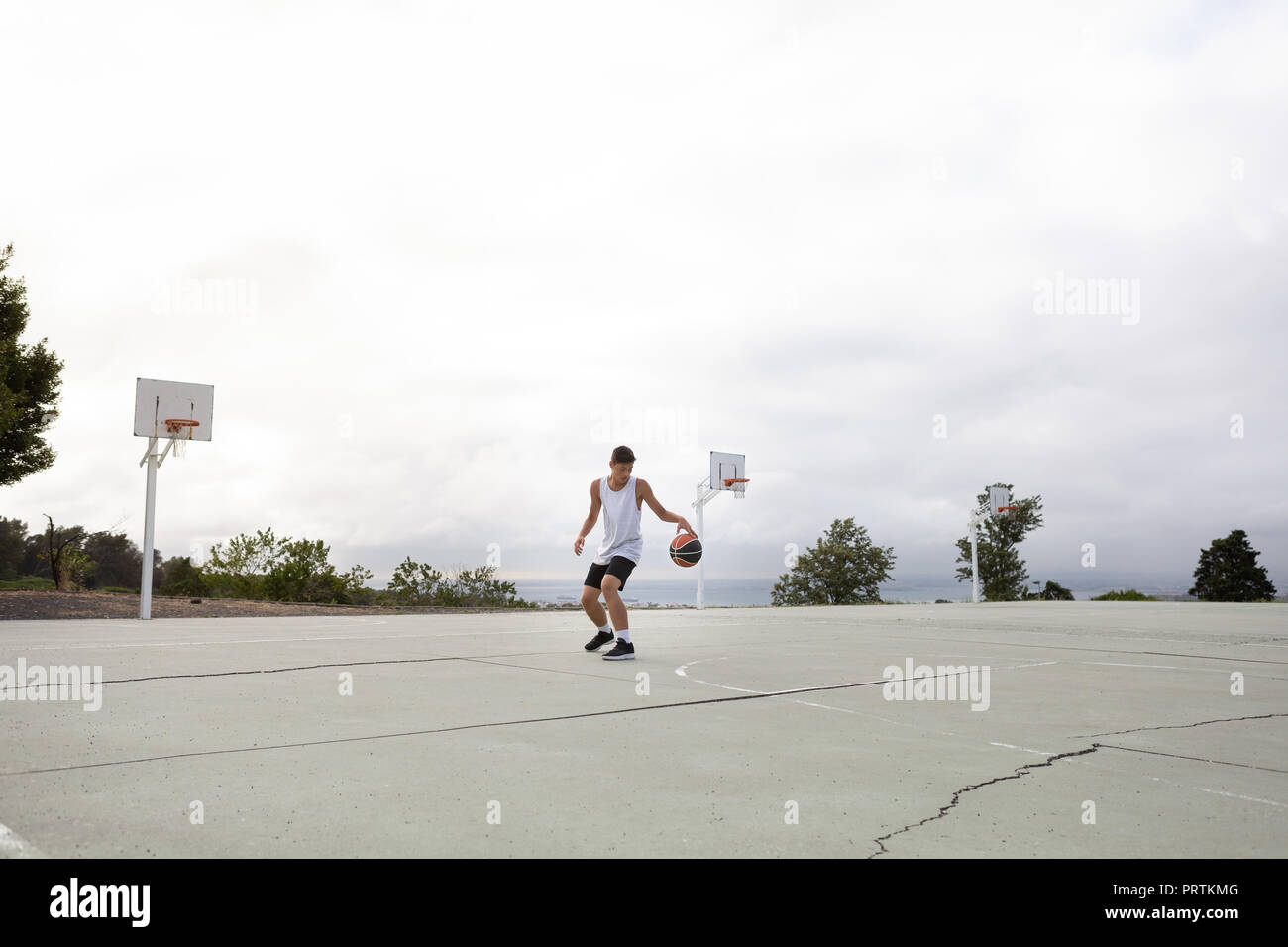 Male teenage basketball player practicing with ball on basketball court ...