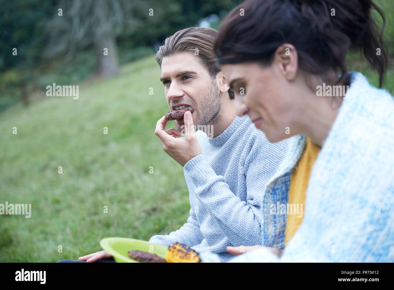 Couple sitting in rural field eating barbecue food Stock Photo - Alamy