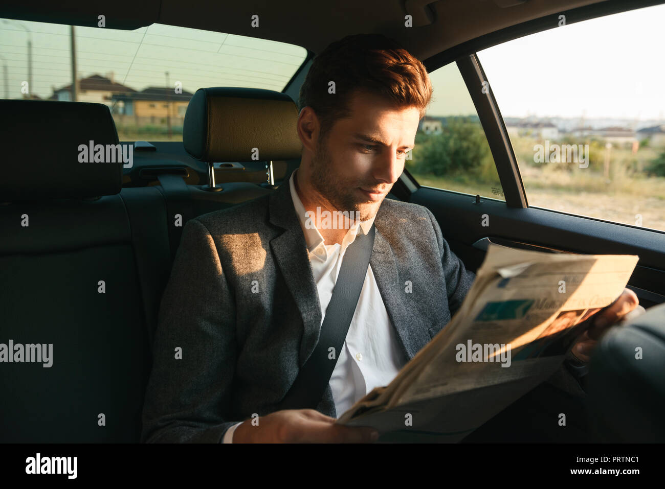 Attractive businessman reading newspaper while sitting at the back of a ...