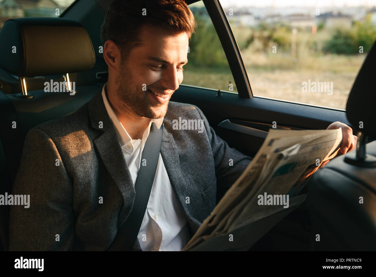 Laughing businessman reading newspaper while sitting at the back of a ...