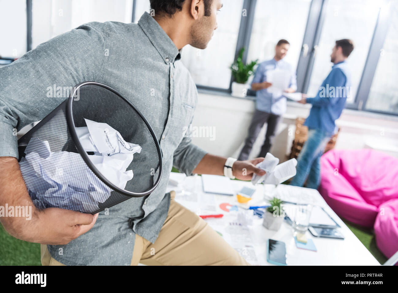 businessman holding trash bucket with papers and looking at coworkers ...