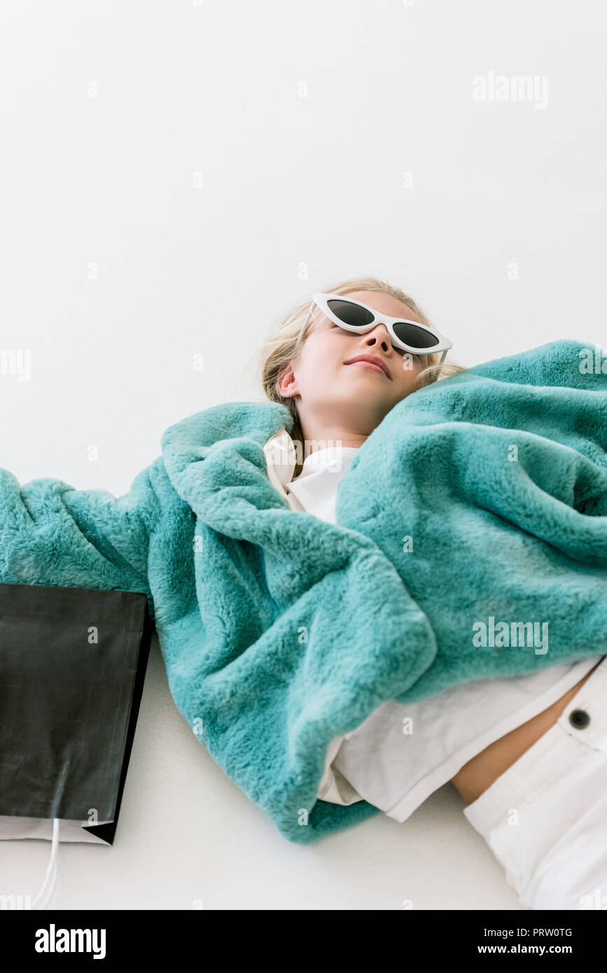 beautiful stylish child in turquoise fur coat lying with black shopping ...