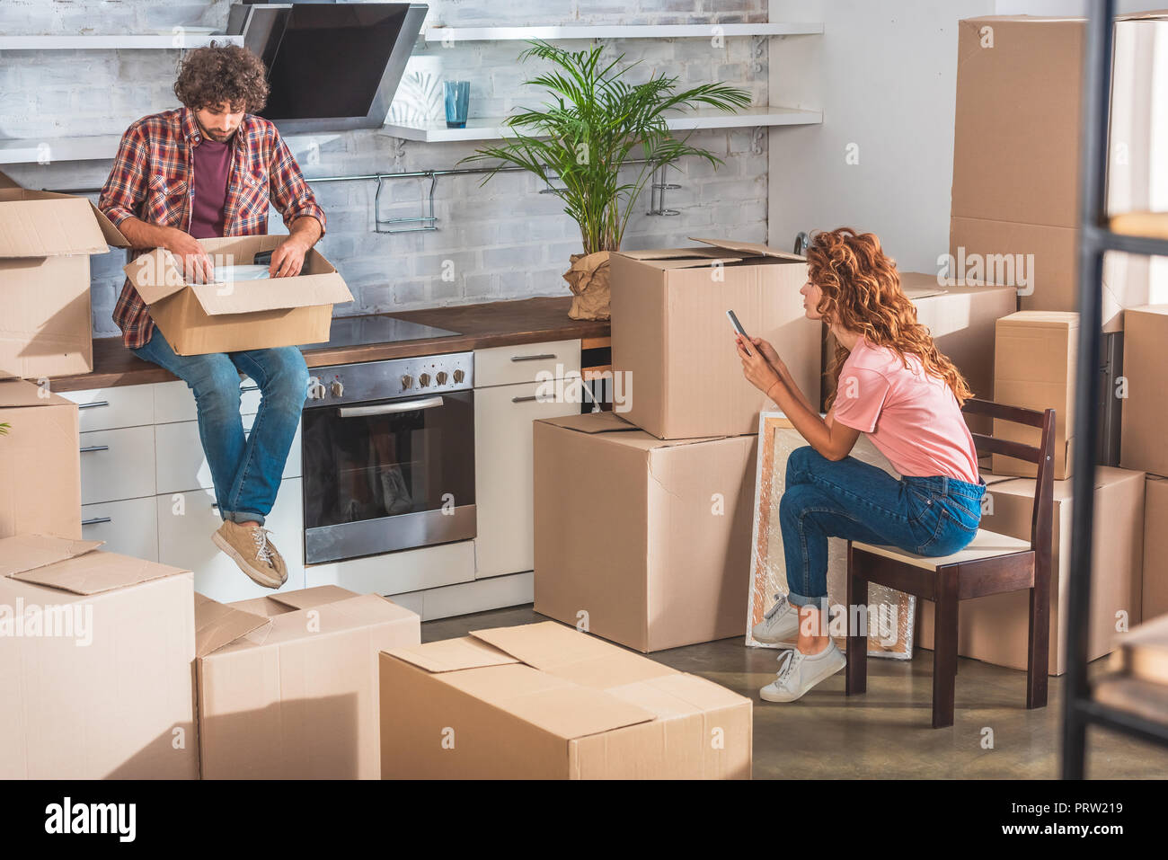 boyfriend unpacking utensil from cardboard box at new home, girlfriend ...