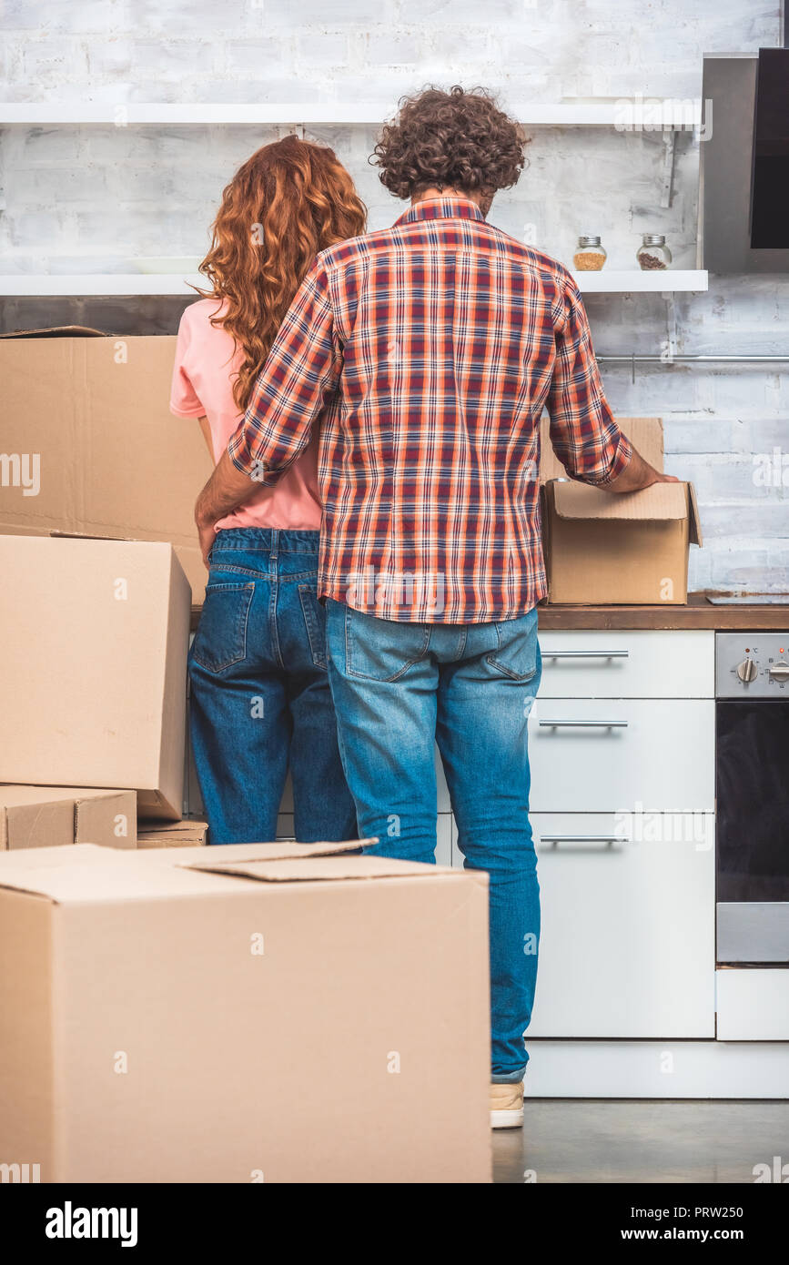 back view of couple hugging and unpacking cardboard box in new kitchen ...