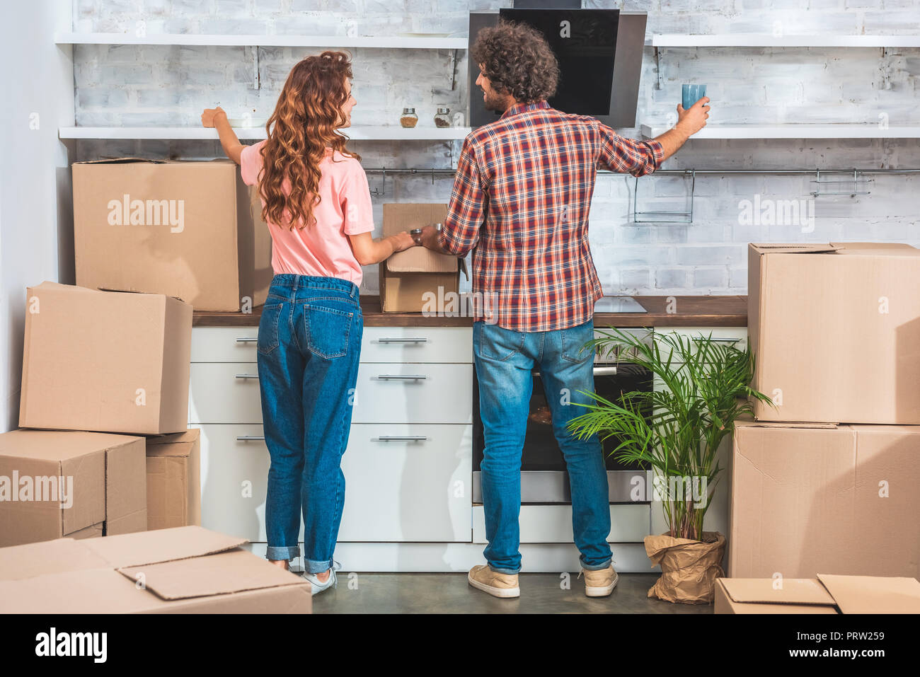back view of couple unpacking cardboard boxes at new home and putting ...