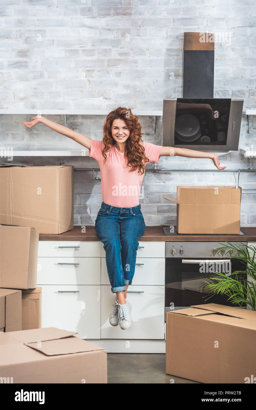 happy beautiful woman sitting on kitchen counter with outstretched ...
