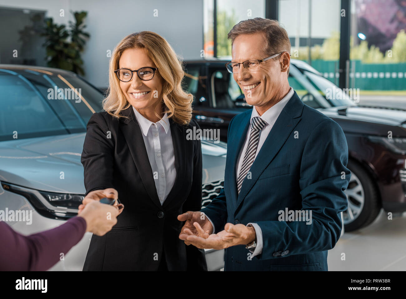 partial view of female car dealer giving car key to smiling couple in ...