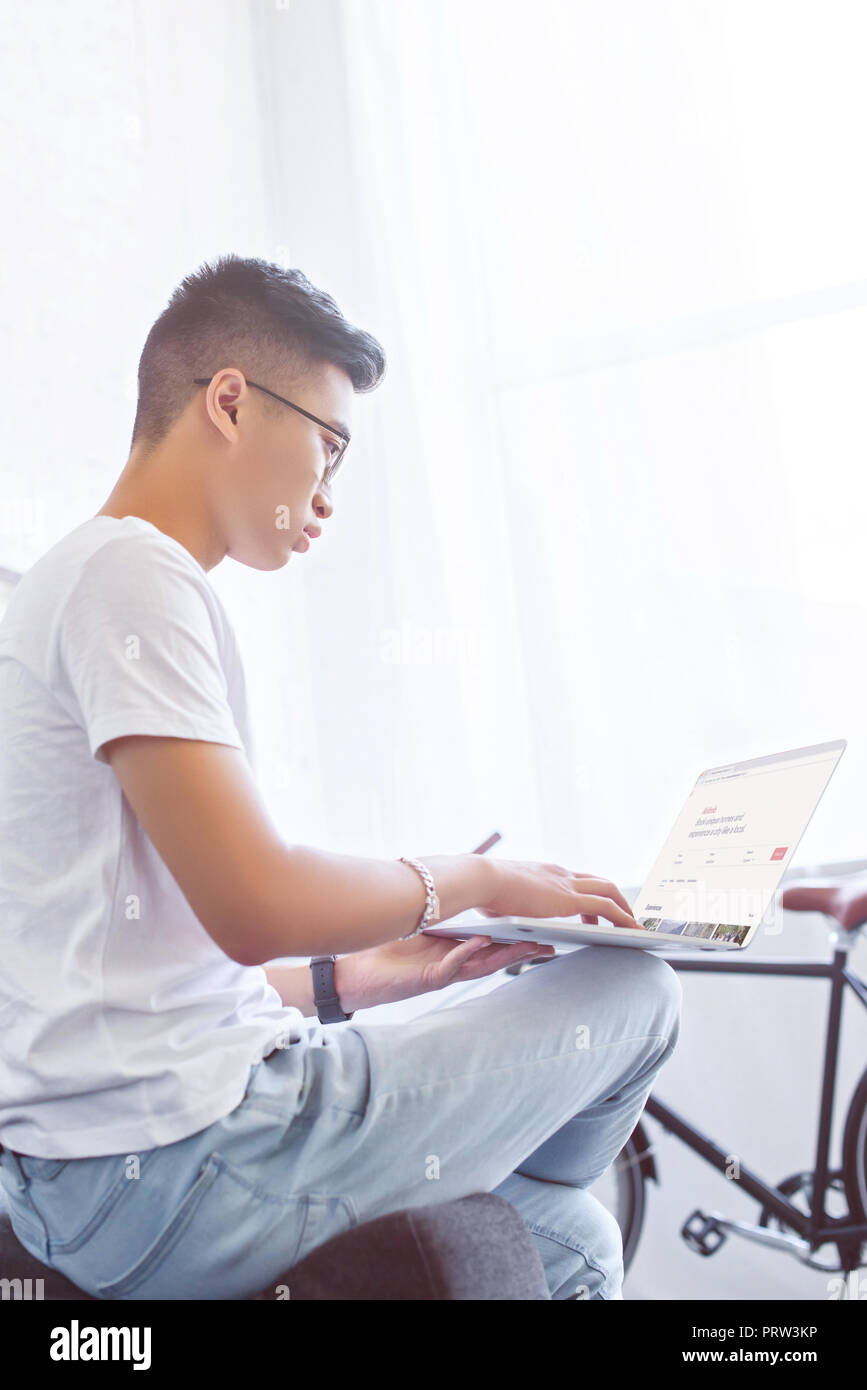 side view of handsome asian man using laptop with loaded airbnb page on ...