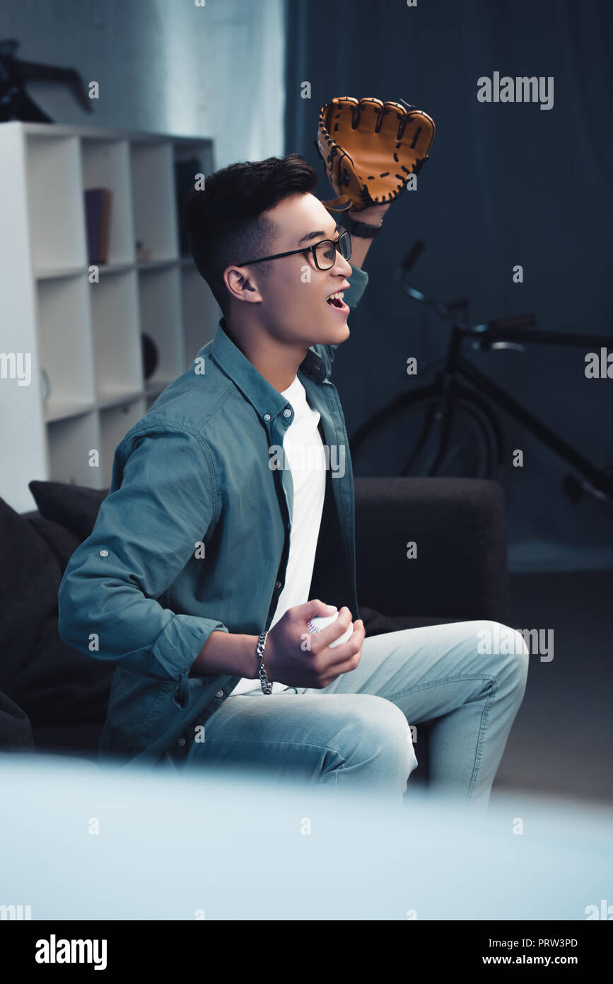 emotional young asian man with baseball glove and ball watching sport ...