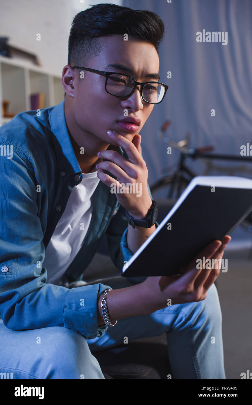 focused young asian man in eyeglasses reading book at home Stock Photo ...