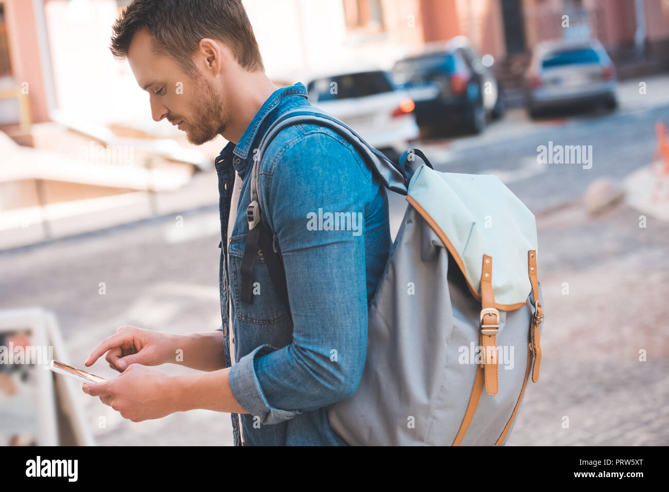 handsome young man with backpack walking by street and using smartphone ...