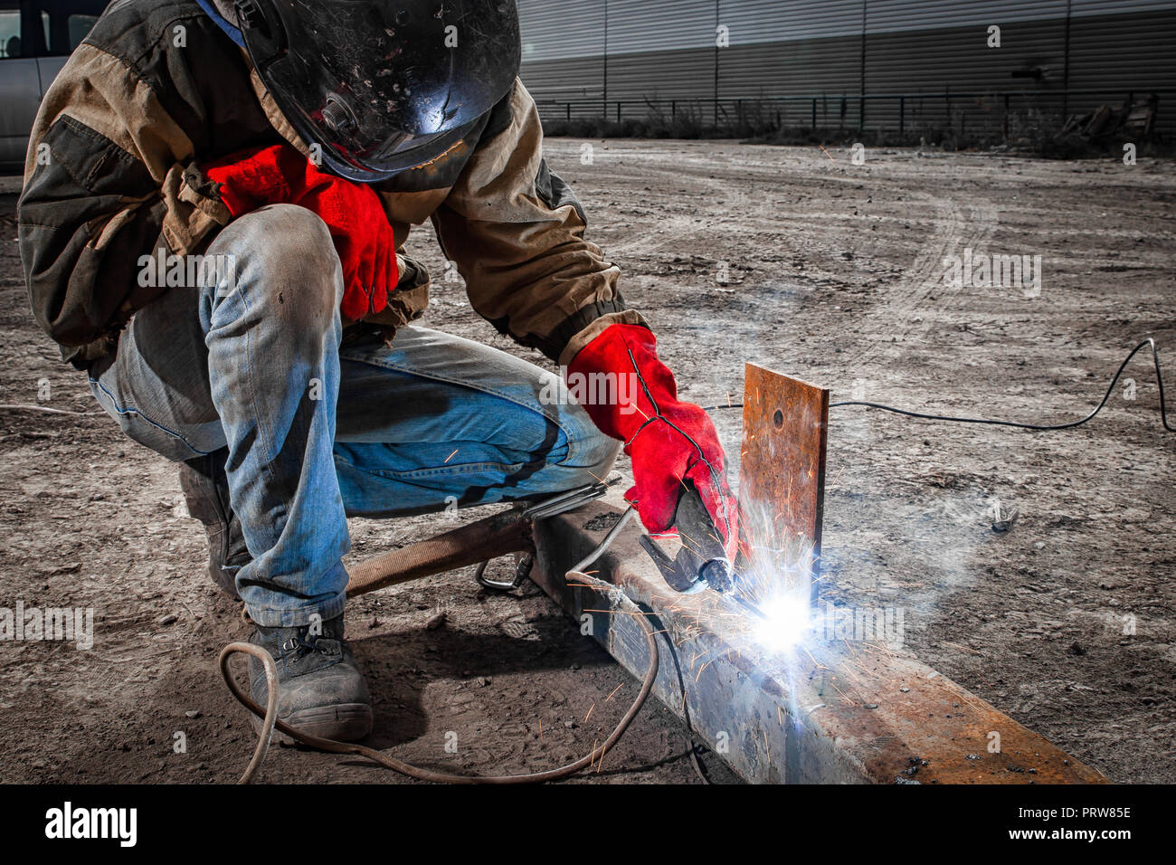 A strong man is a welder in brown uniform, welding mask and welders ...