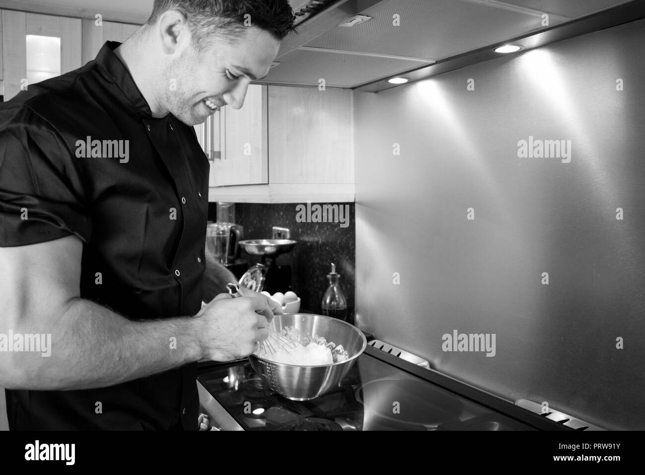 Handsome, smiling and laughing chef wearing black chef's jacket mixes ...