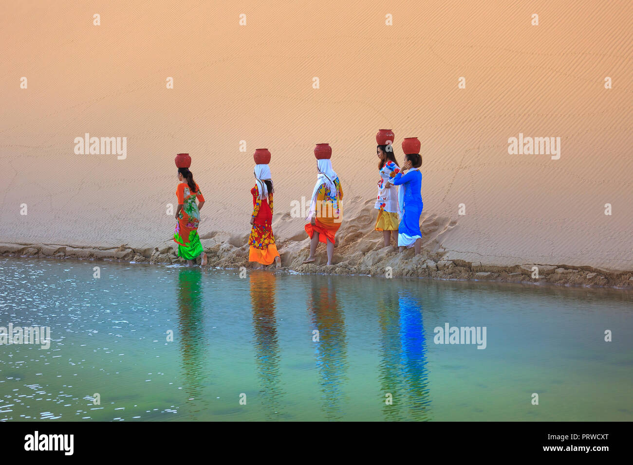 Cham women in traditional dress walking across sand dunes to collecting ...