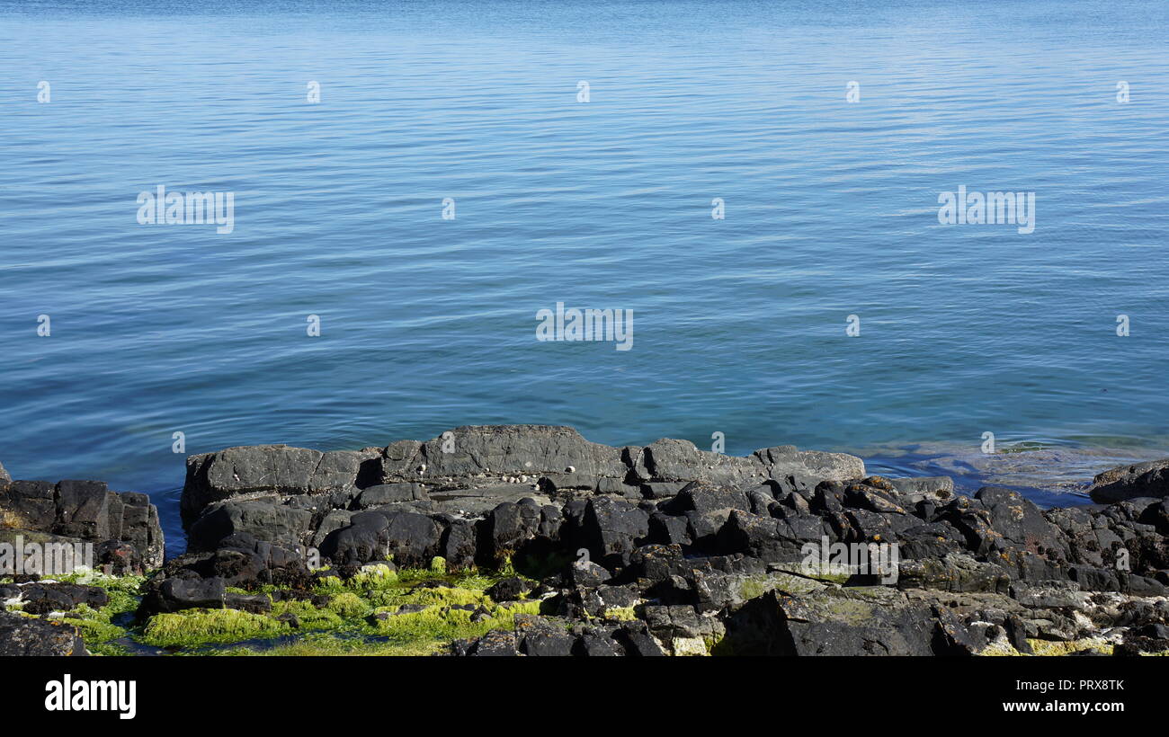 Blue infinity calming water at a rocky shoreline Stock Photo - Alamy