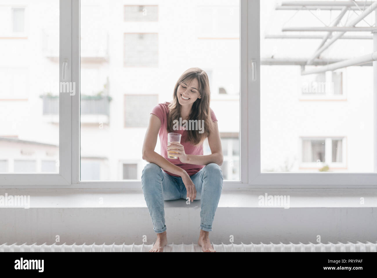 Woman sitting on window sill, holding a glass Stock Photo - Alamy