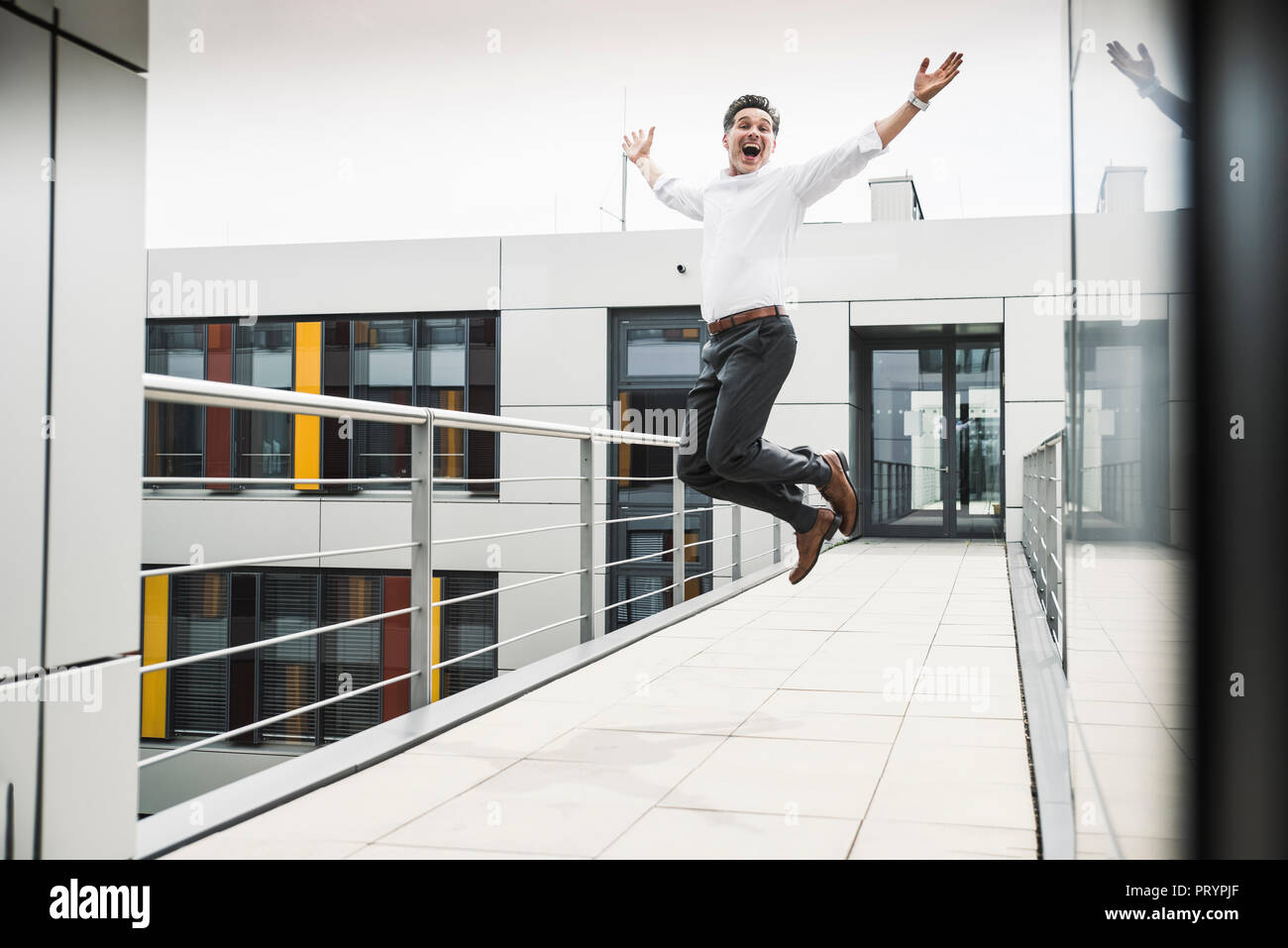 Cheering businessman jumping on skywalk at office building Stock Photo ...