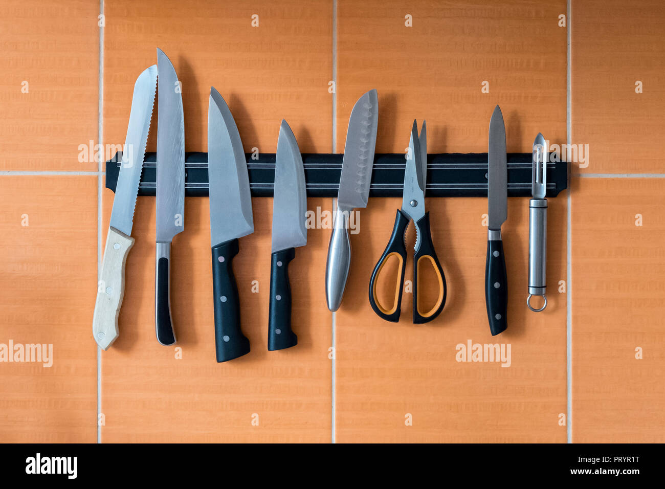 Knives hang on a magnet holder. Orange kitchen wall. A method of ...