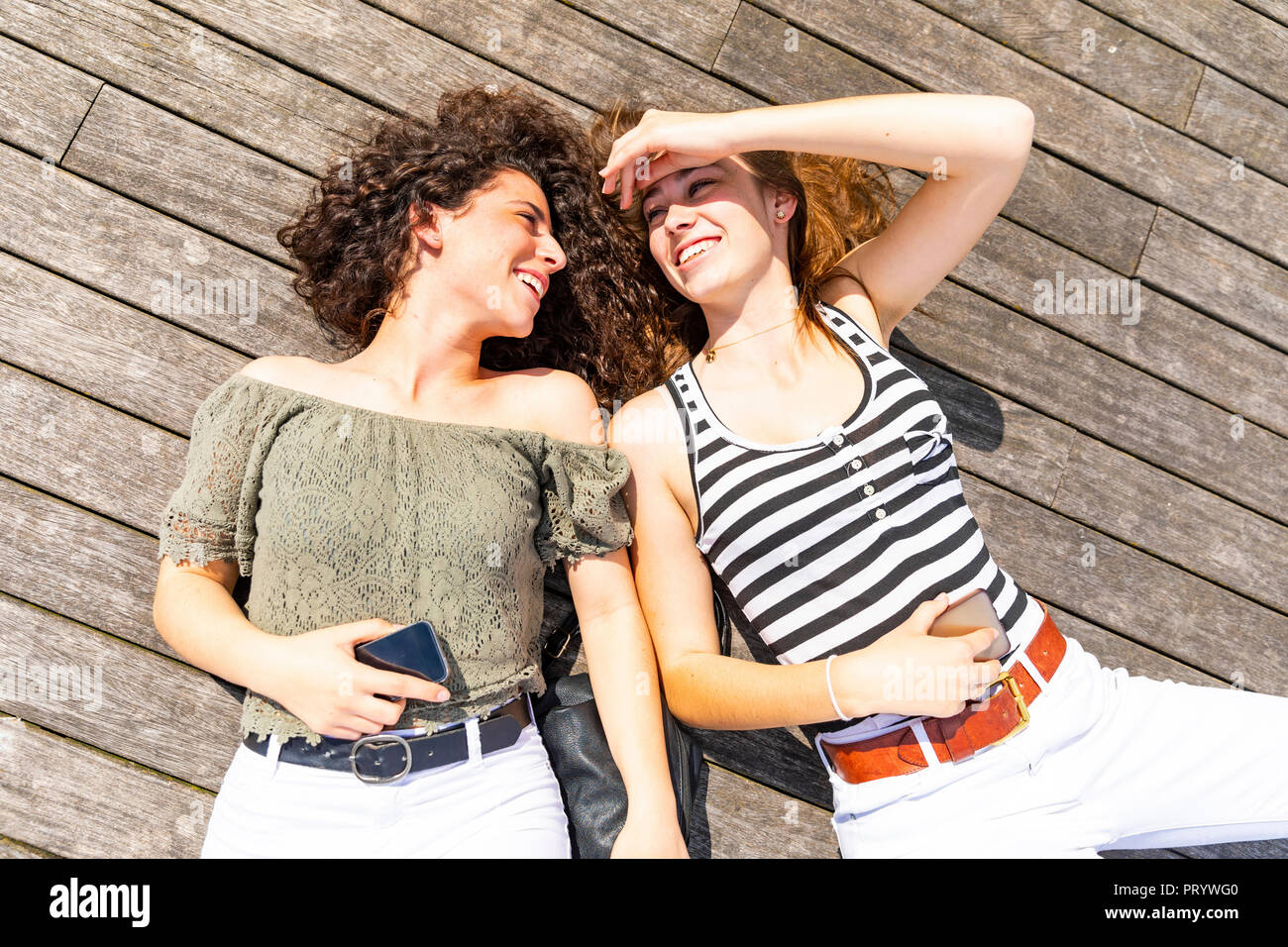 Two happy female friends lying down on a wooden floor Stock Photo - Alamy