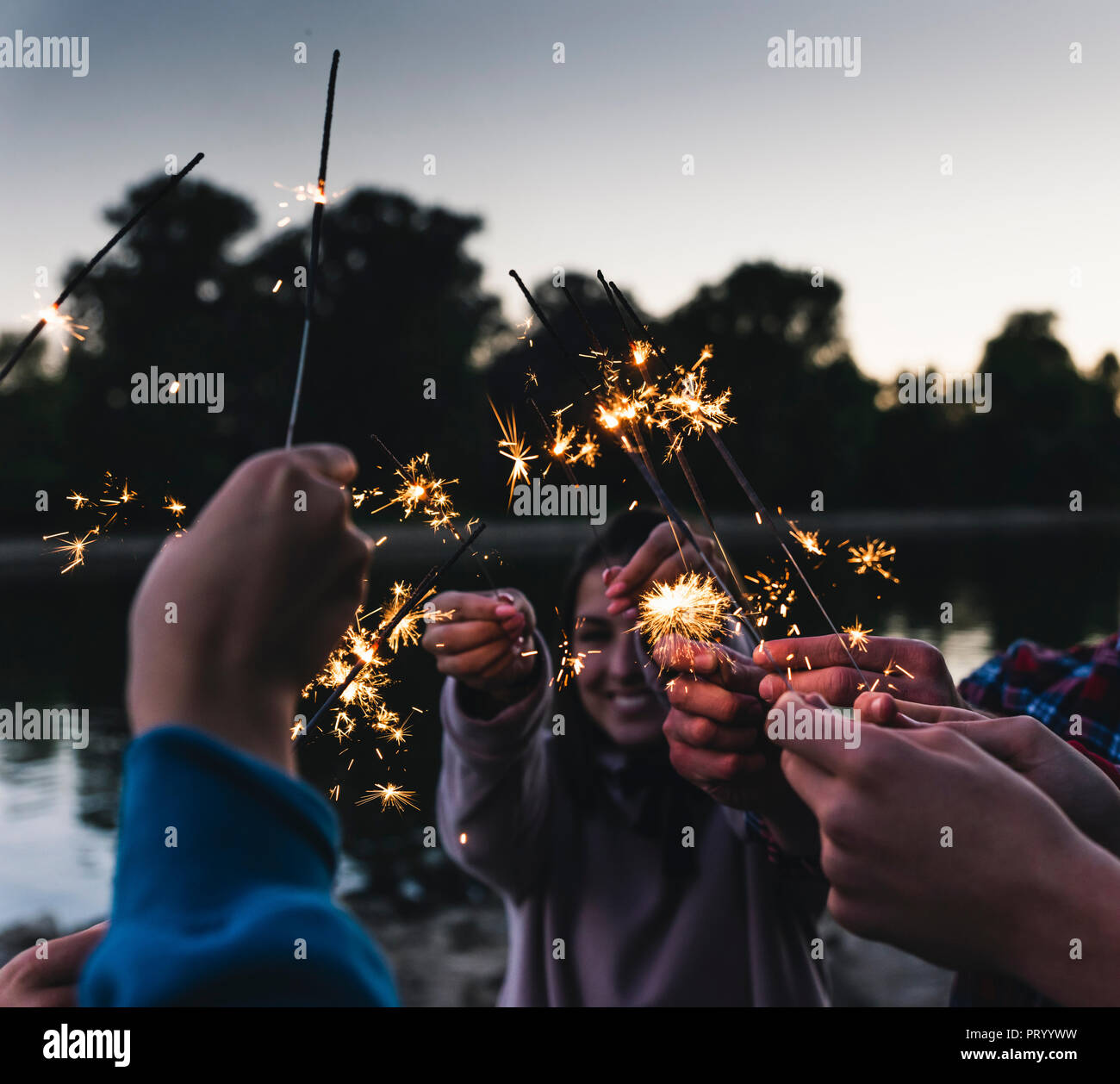 Group of friends at the riverside holding sparklers in the evening ...