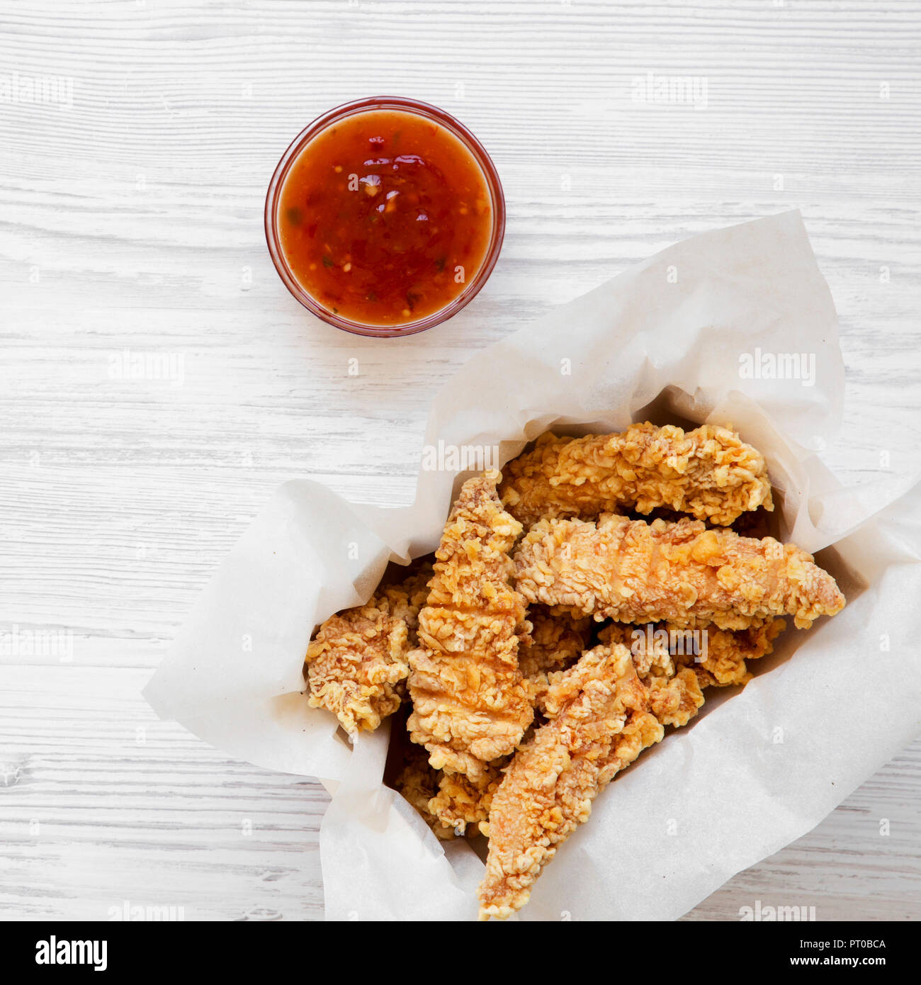 Chicken tenders in paper box with sauce on a white wooden background ...
