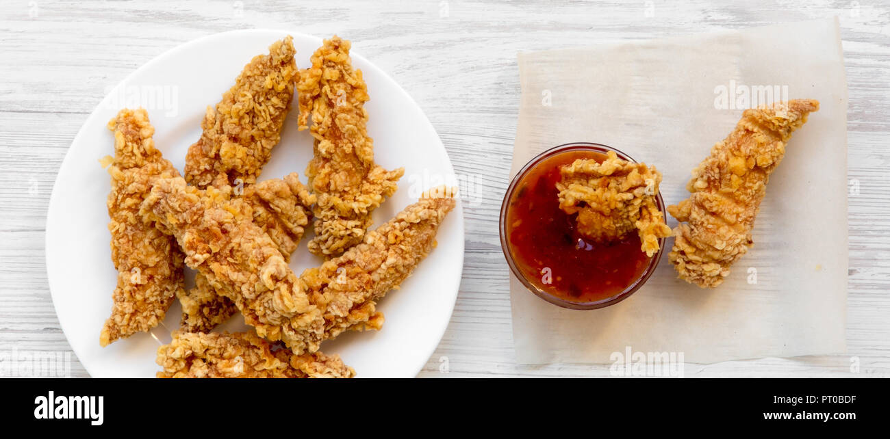 Spicy chicken strips on white plate with sauce over white wooden ...