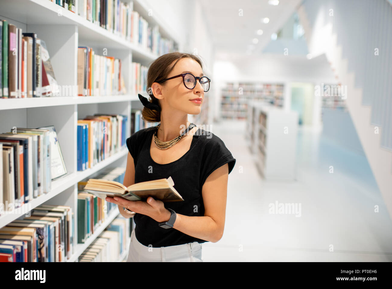 Young woman searching books at the modern library interior with white ...