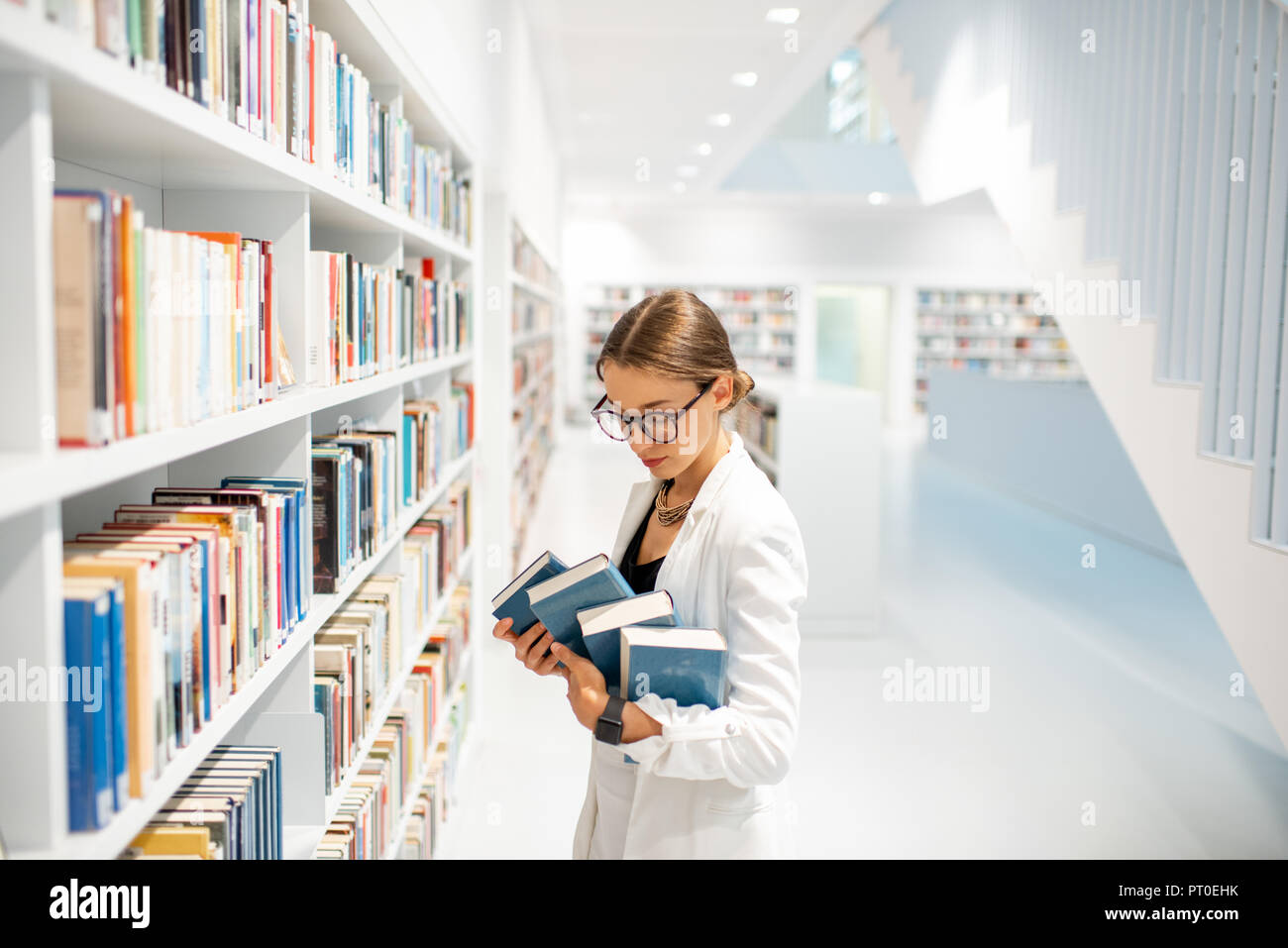 Young businesswoman searching books standing near the bookshelves at ...