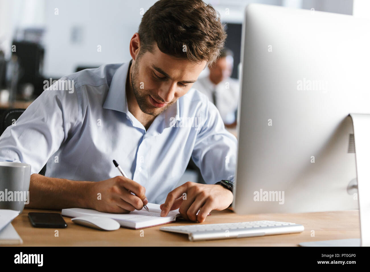 Image of Calm male manager writing something while sitting by the table ...