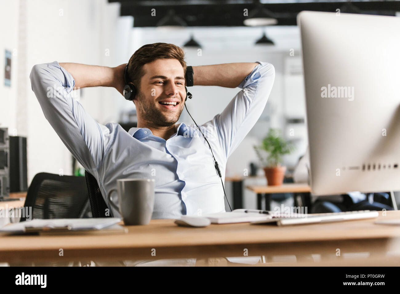 Smiling office manager talking by headset with microphone while sitting ...