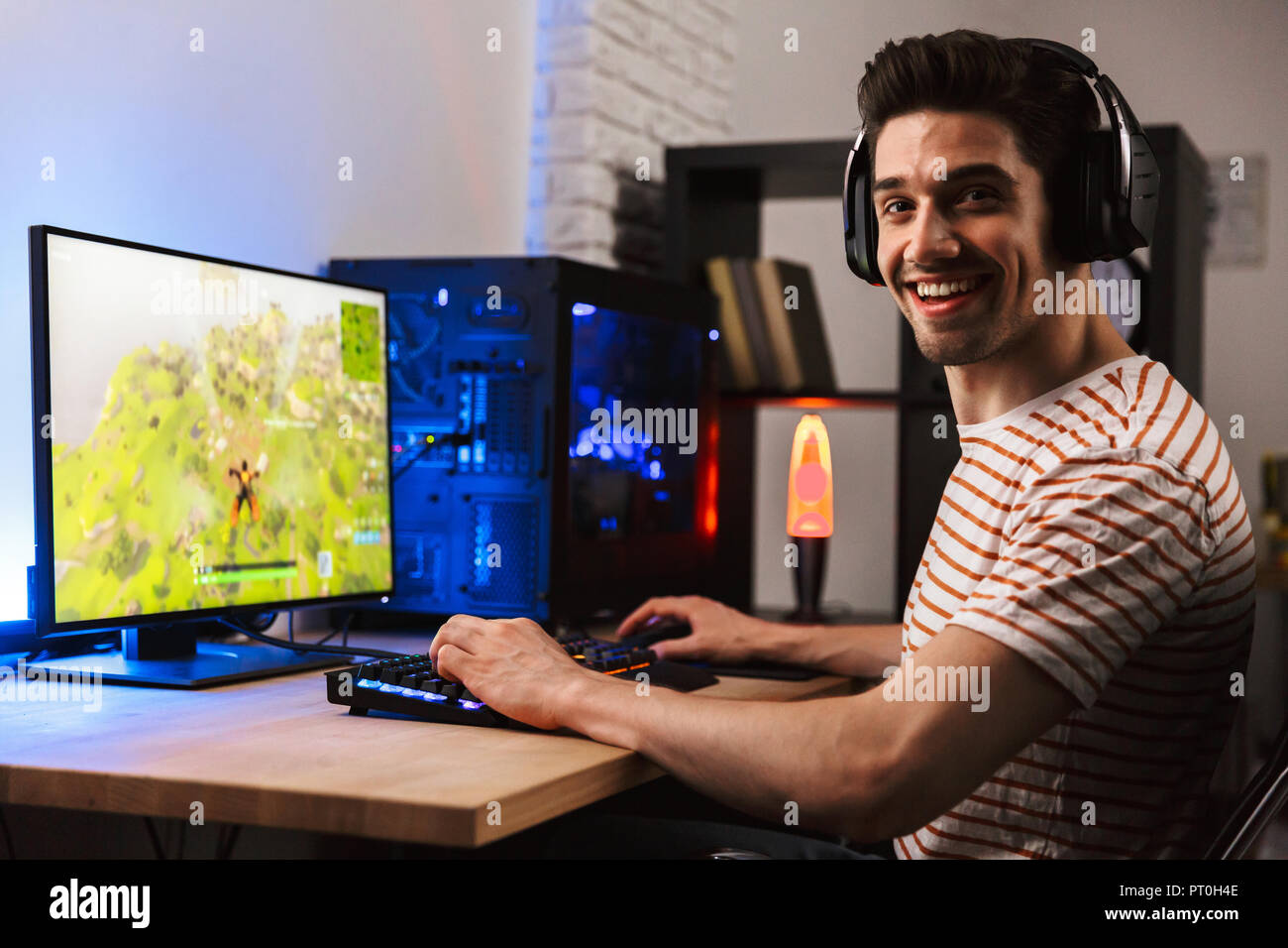 Portrait of happy smiling guy playing video games on computer wearing ...